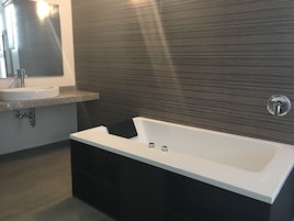 Casa de banho moderna com banheira branca, pia e espelho.