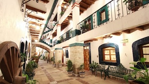 Interior com vários níveis, uma escadaria central, pilares de pedra e plantas em vasos.