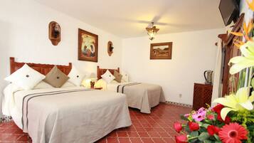 Quarto de hotel com duas camas, televisão, ventoinha no teto e arranjo de flores.