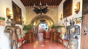 Um corredor com armaduras medievais expostas, um candelabro e um arco de pedra.
