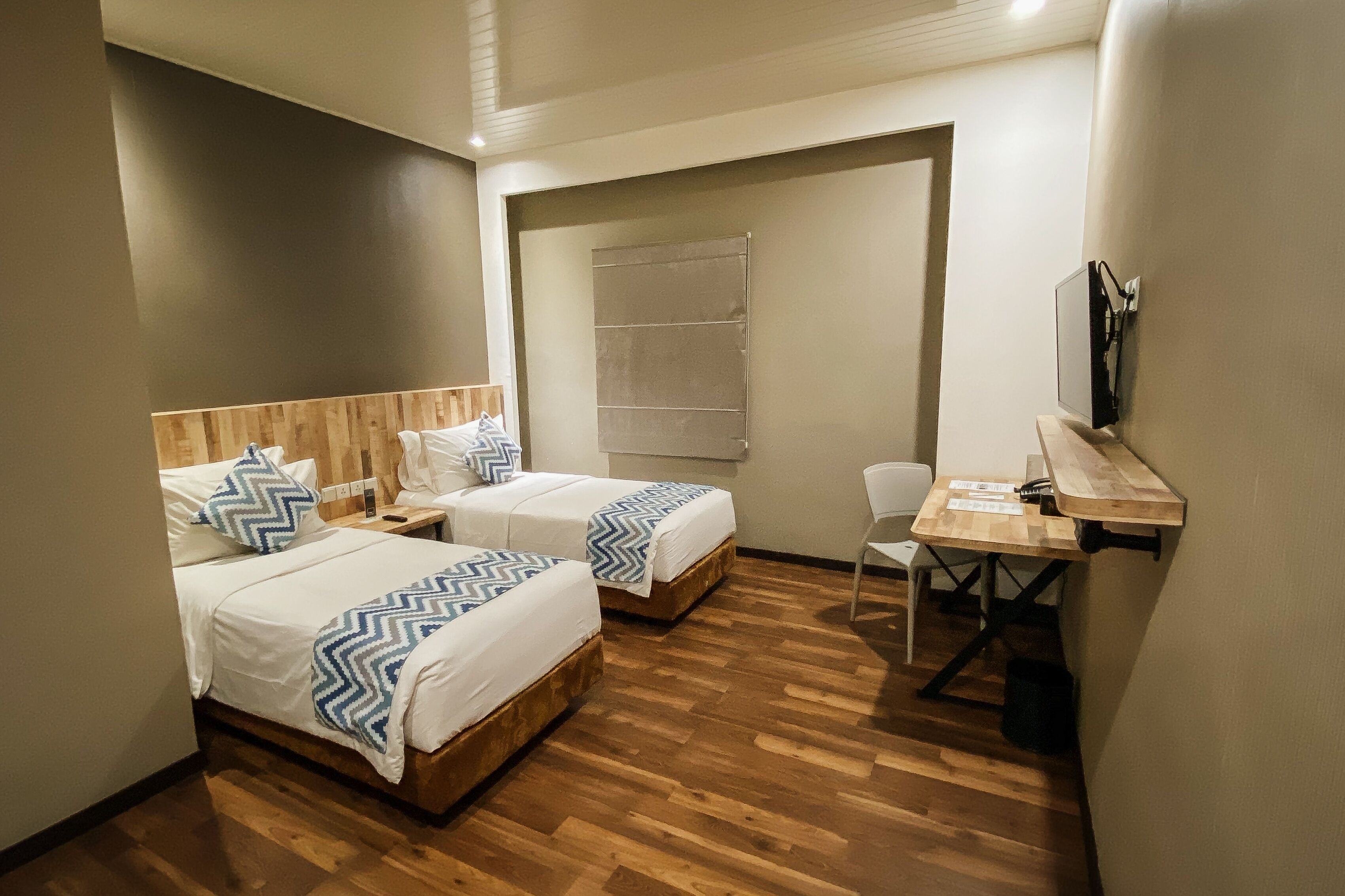 Quarto de hotel com duas camas, uma escrivaninha e uma cadeira.