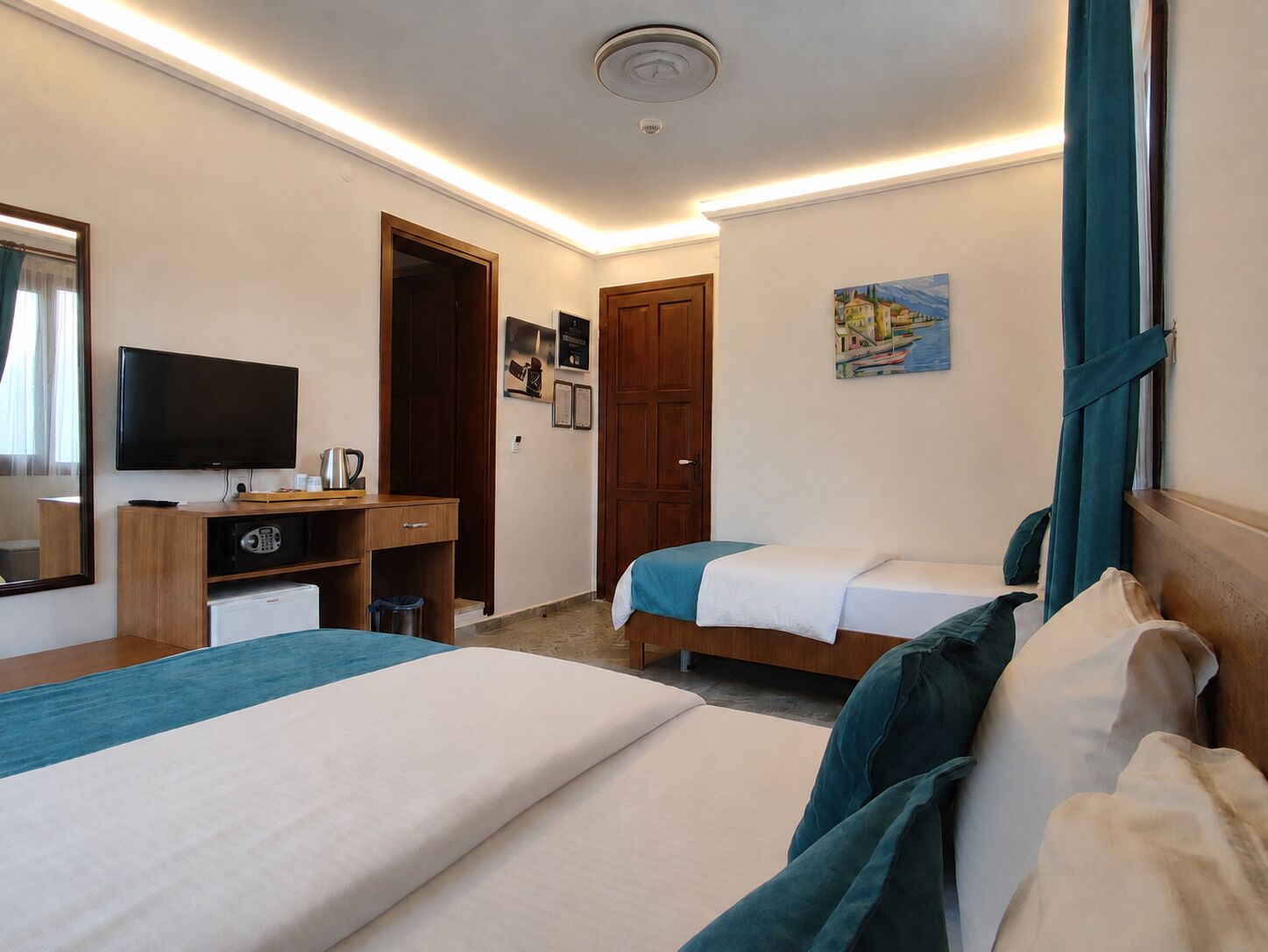 Quarto de hotel com duas camas, uma secretária com televisão, máquina de café e um quadro na parede.