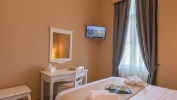 Quarto de hotel com uma cama grande, uma escrivaninha com cadeira, uma televisão na parede e uma janela com cortinas.
