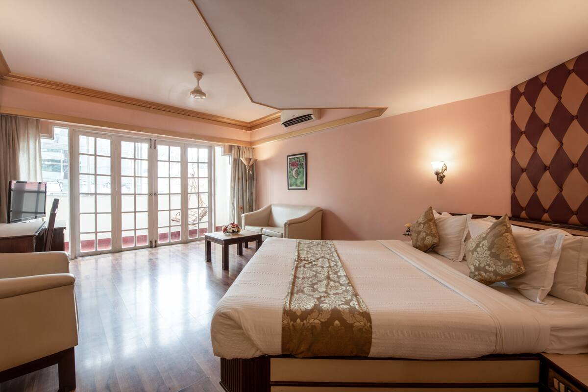 Quarto de hotel com uma cama grande, uma escrivaninha, uma cadeira e vista da cidade por grandes janelas.