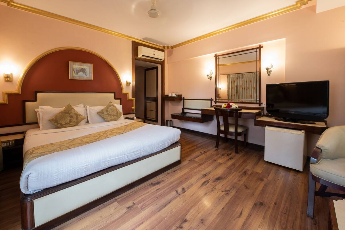 Quarto de hotel com uma cama grande, uma mesa de trabalho com televisão, uma cadeira e um pequeno frigorífico.