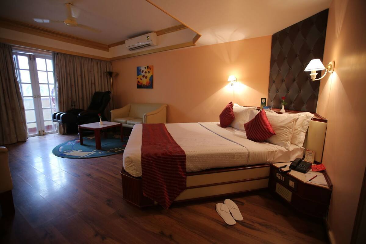 Quarto de hotel com cama, mesa de cabeceira, luminária, cadeira e uma pequena mesa.