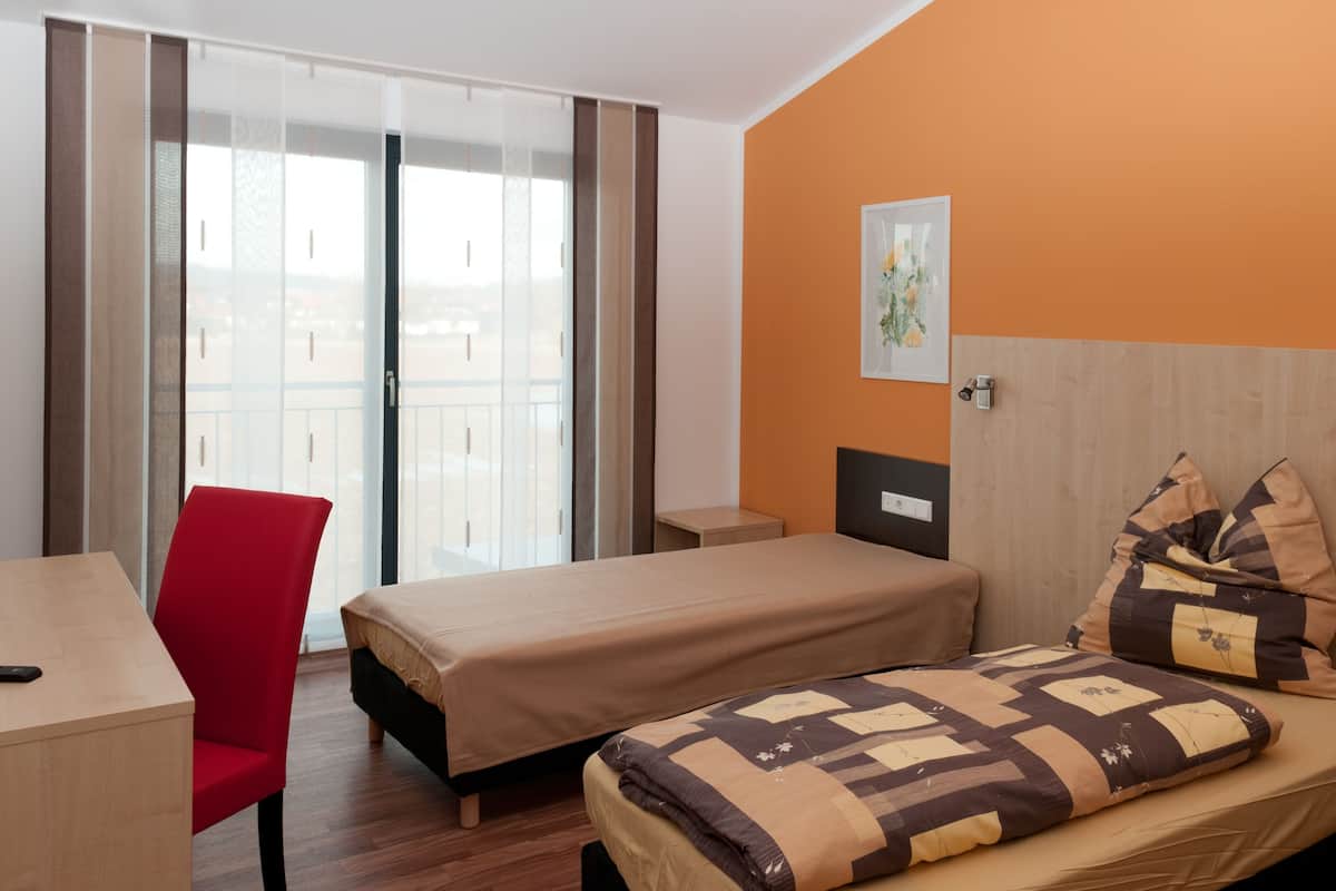 Quarto de hotel com cama, secretária, cadeira e janela com cortinas.