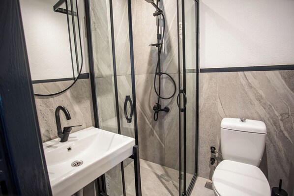 Casa de banho moderna com lavatório branco, acessórios em preto e cabine de duche em vidro.
