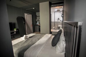 Quarto de hotel moderno com cama, um espelho grande, banheiro com chuveiro e uma pequena cozinha.