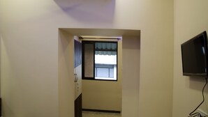 Quarto com ar condicionado, uma pequena janela com cortinas e televisão fixada na parede.
