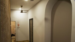 Um corredor com assoalho de madeira, ventilador de teto, uma porta e um pequeno armário com um objeto vermelho.