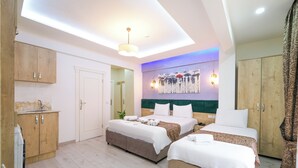 Quarto de hotel com duas camas, um guarda-roupa de madeira, uma kitchenette pequena e uma luminária no teto.