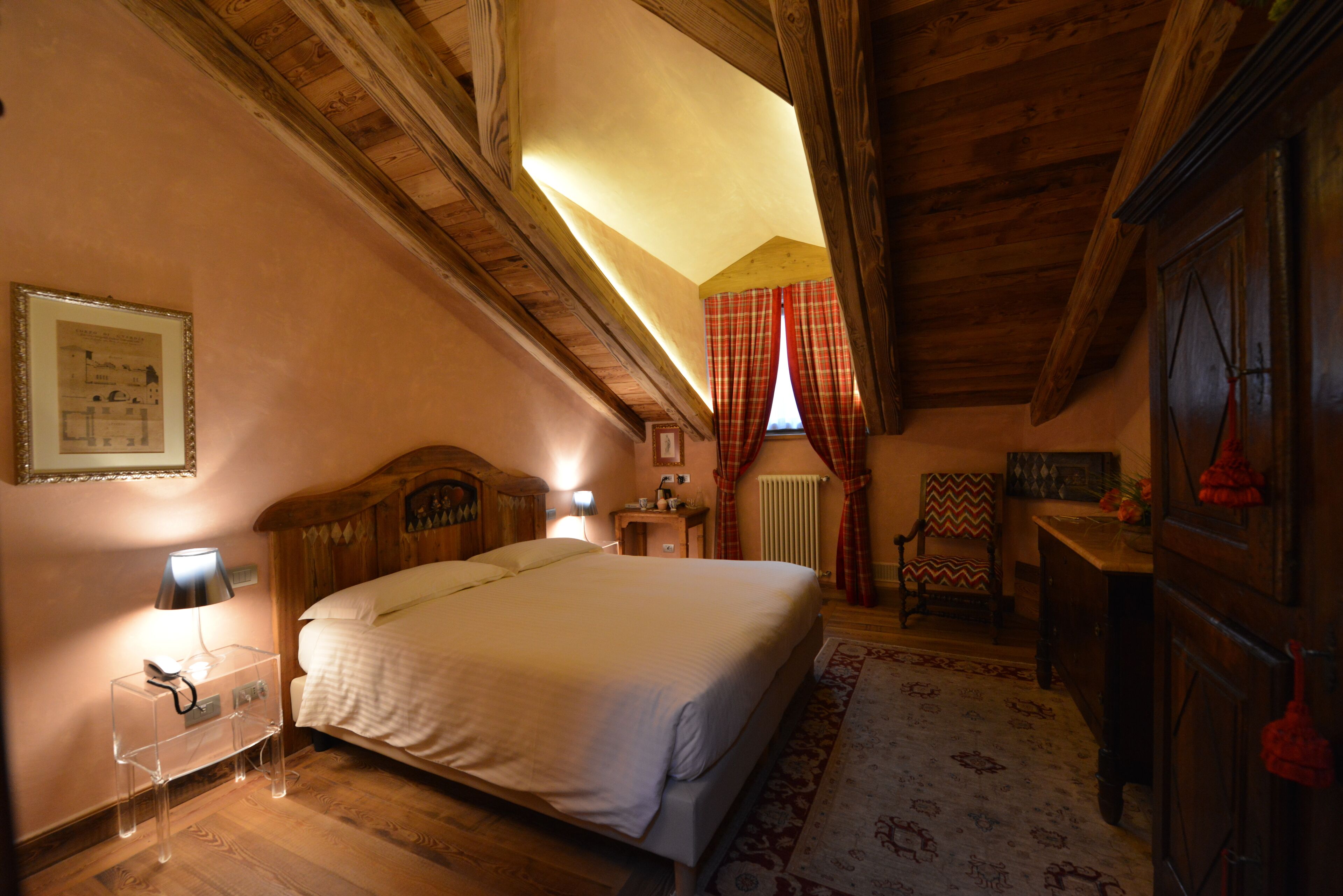 Quarto com teto de madeira, uma cama, mesa de cabeceira com abajur, uma cadeira e um aparador.