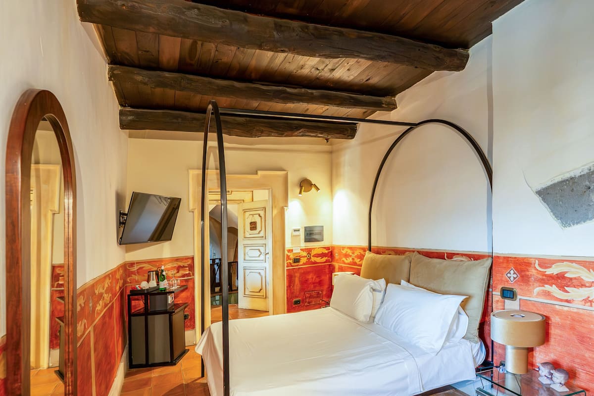 Um quarto com uma cama, mesa de cabeceira, espelho, guarda-roupa e uma porta.