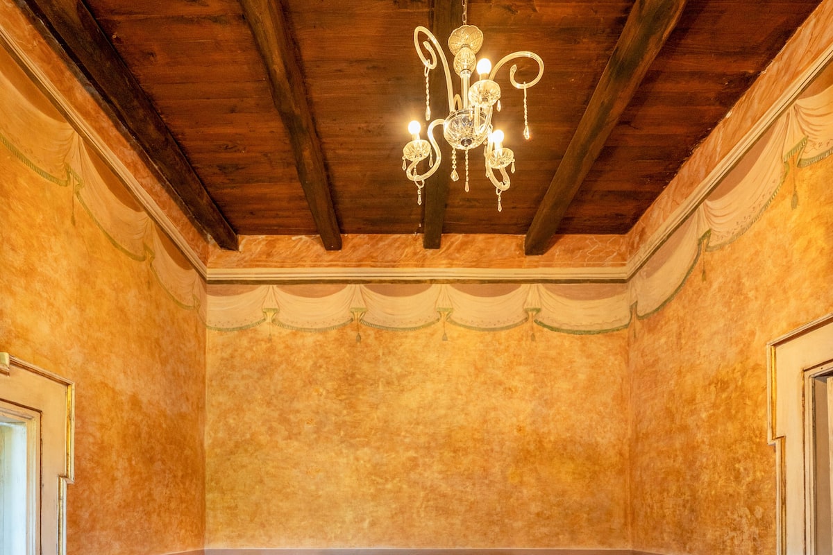 Um quarto espaçoso com uma cama grande, vigas de madeira no teto e um candelabro.