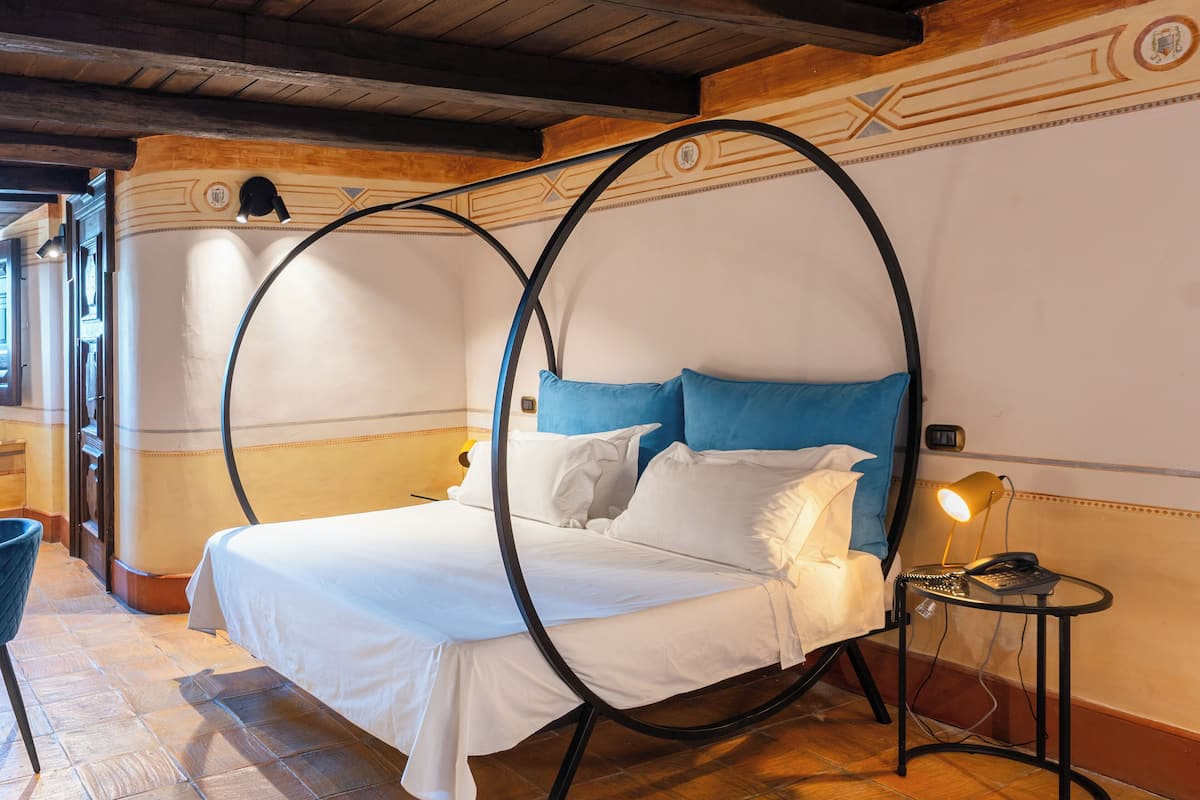 Uma cama de dossel com lençóis brancos, cabeceira azul e mesa de cabeceira com abajur e telefone.
