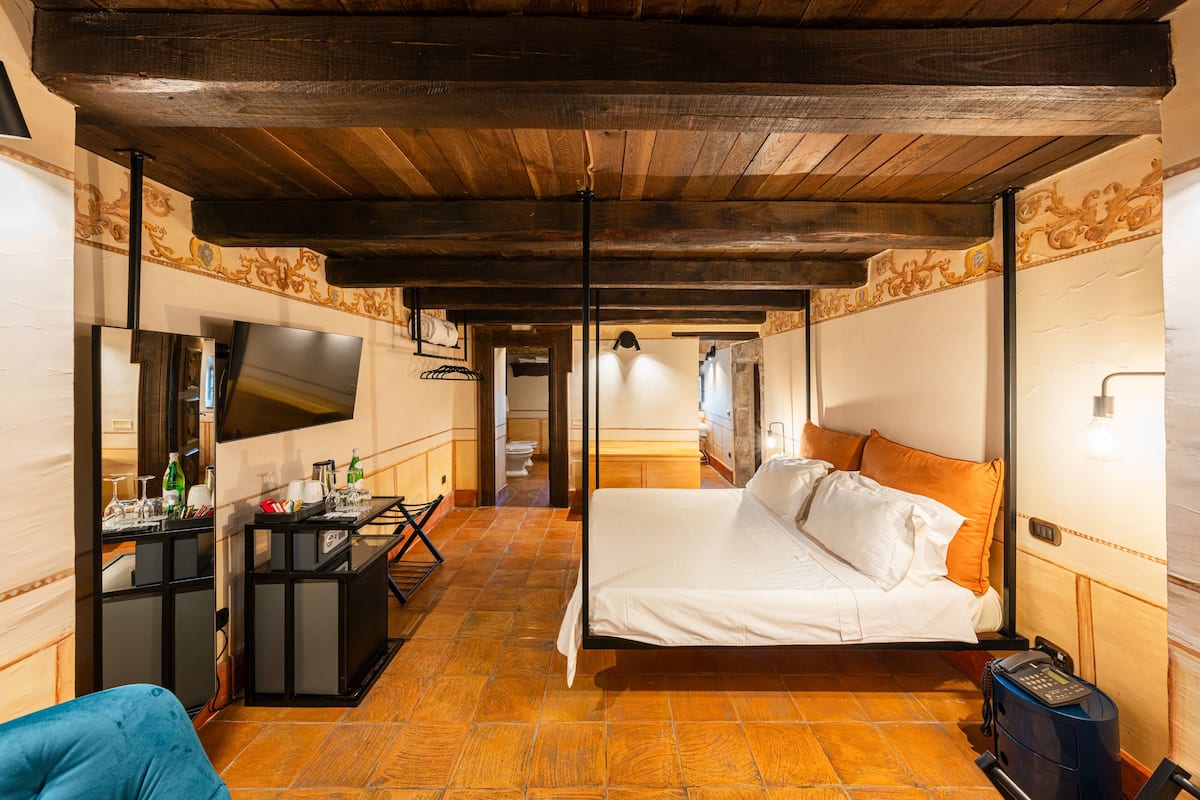 Quarto de hotel com cama, secretária com televisão de tela plana, minibar e banheiro visível por uma porta aberta.