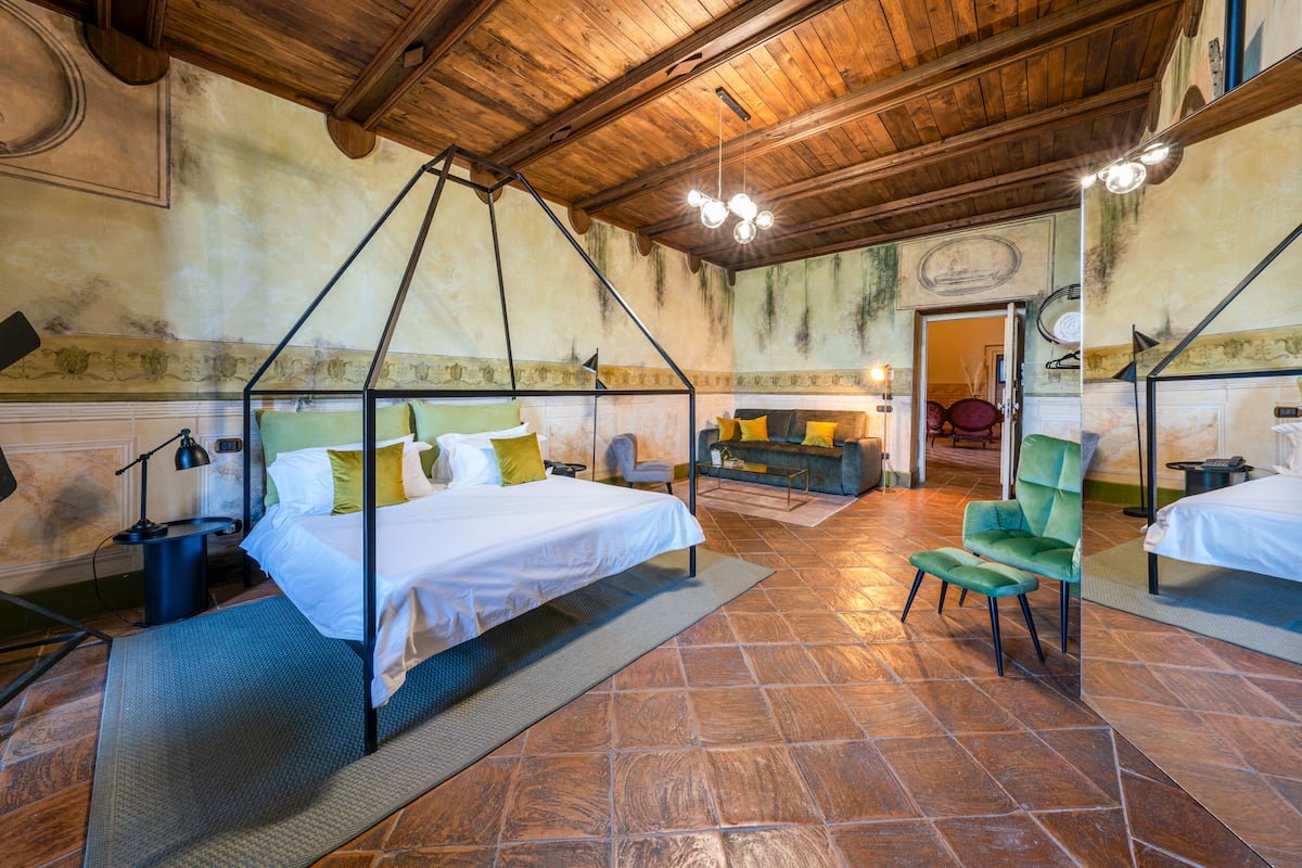 Quarto com uma cama de dossel, uma poltrona verde e um sofá.