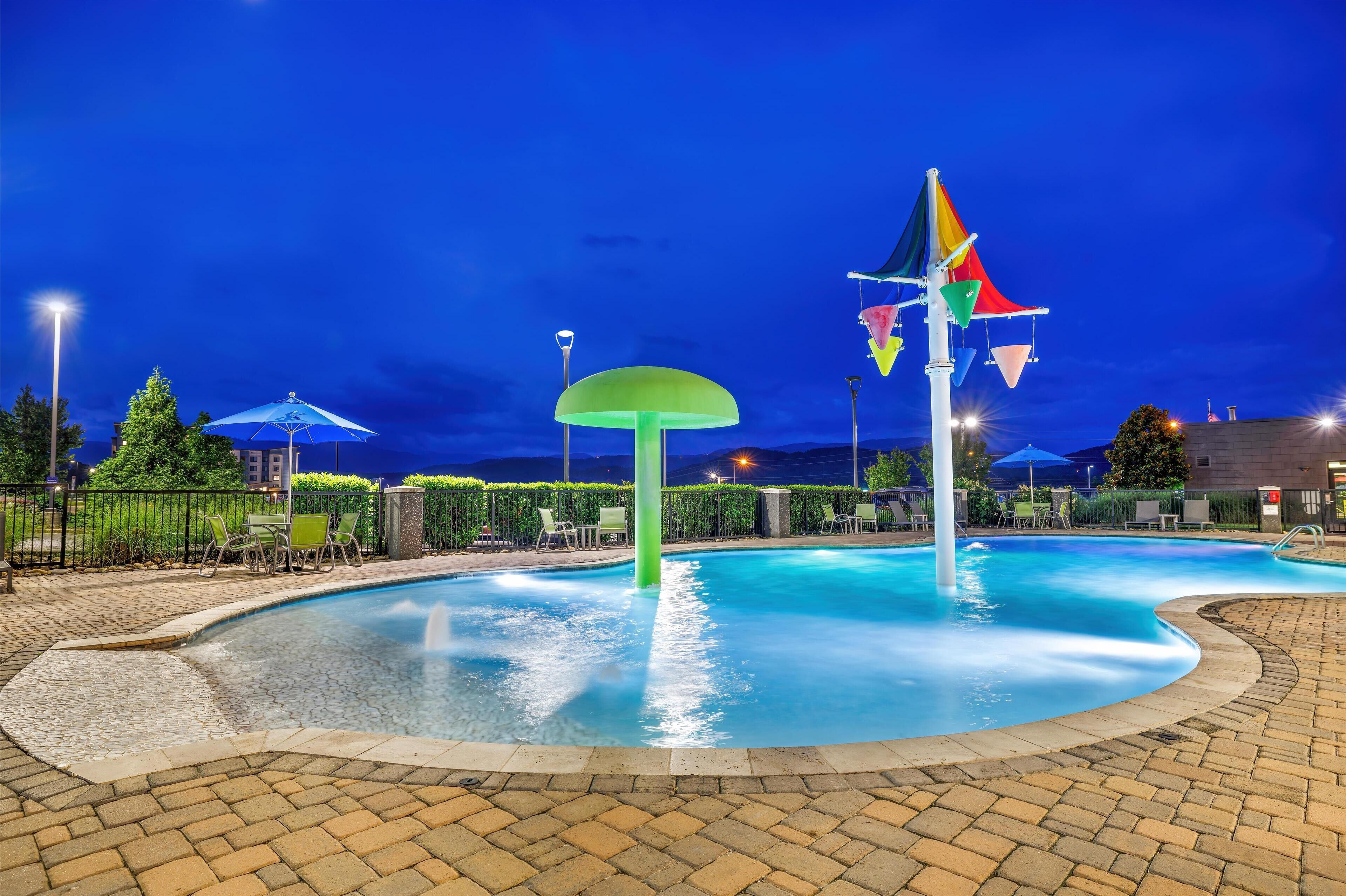 Piscina com fonte, rodeada por um pátio de tijolos e cadeiras verdes.