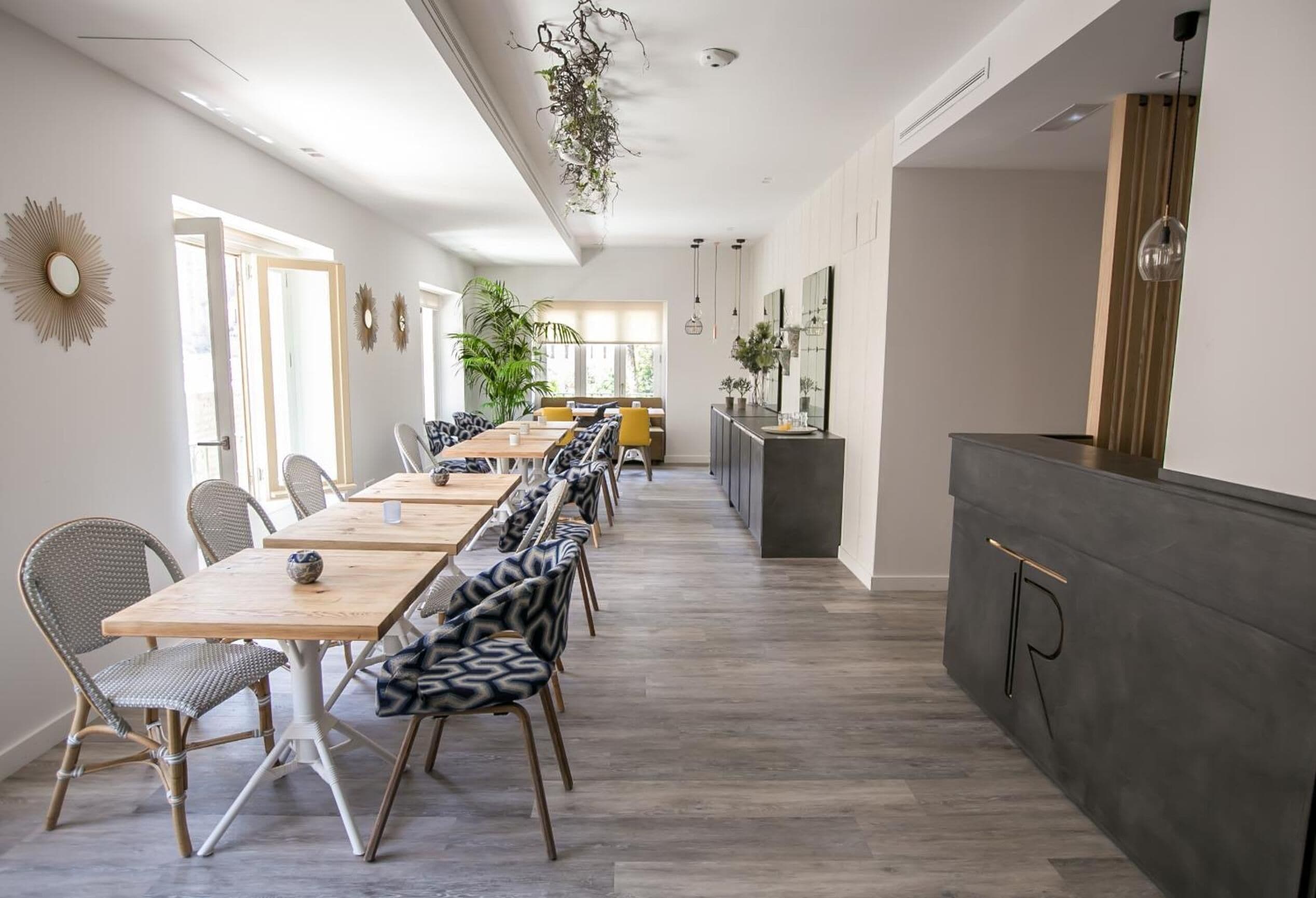 Uma sala de jantar moderna com uma mesa de madeira comprida, cadeiras estampadas e um espaço de bar com balcão e plantas.