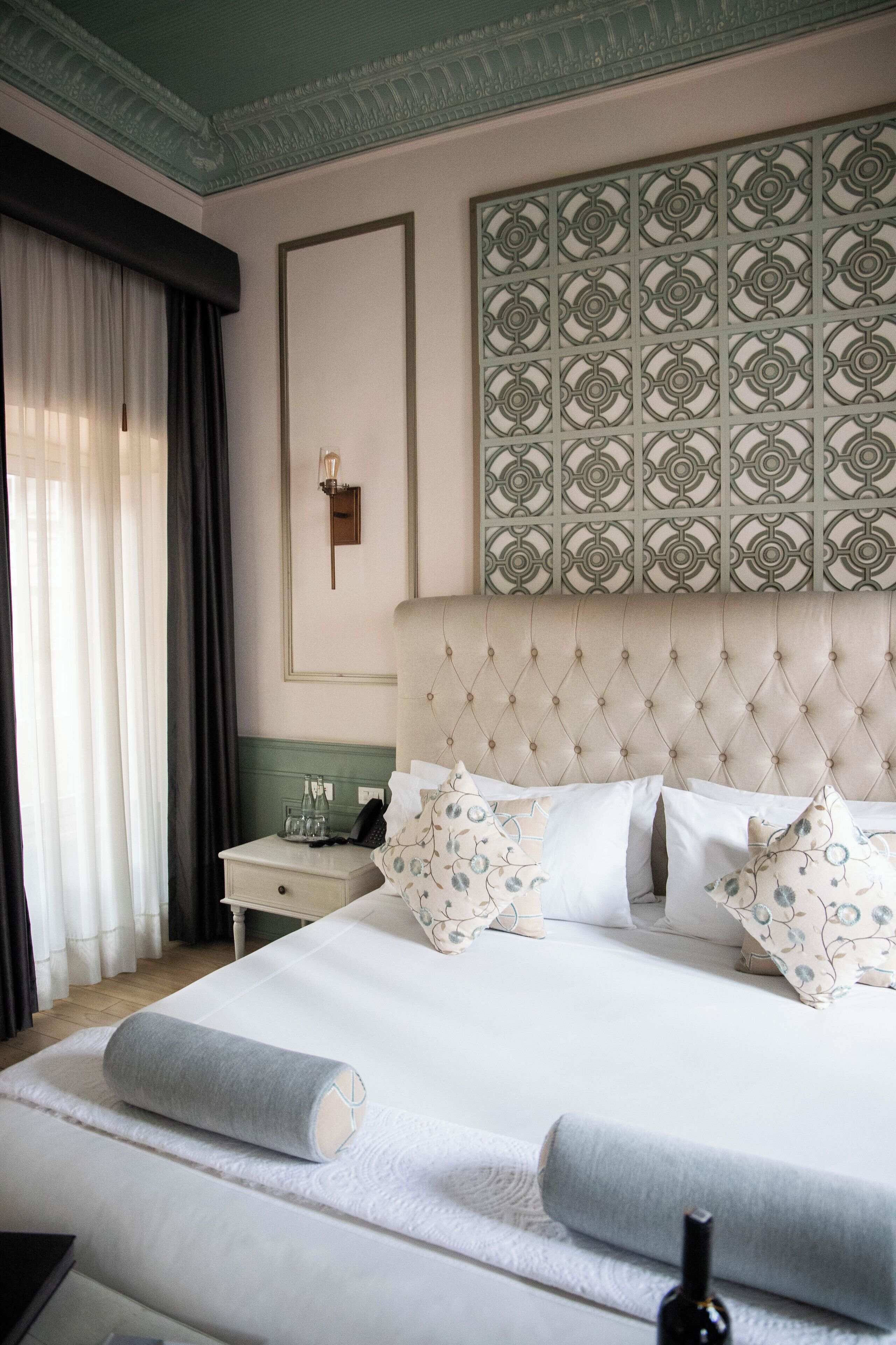 Uma cama bem arrumada com cabeceira estofada, mesa de cabeceira com abajur e painel decorativo na parede.