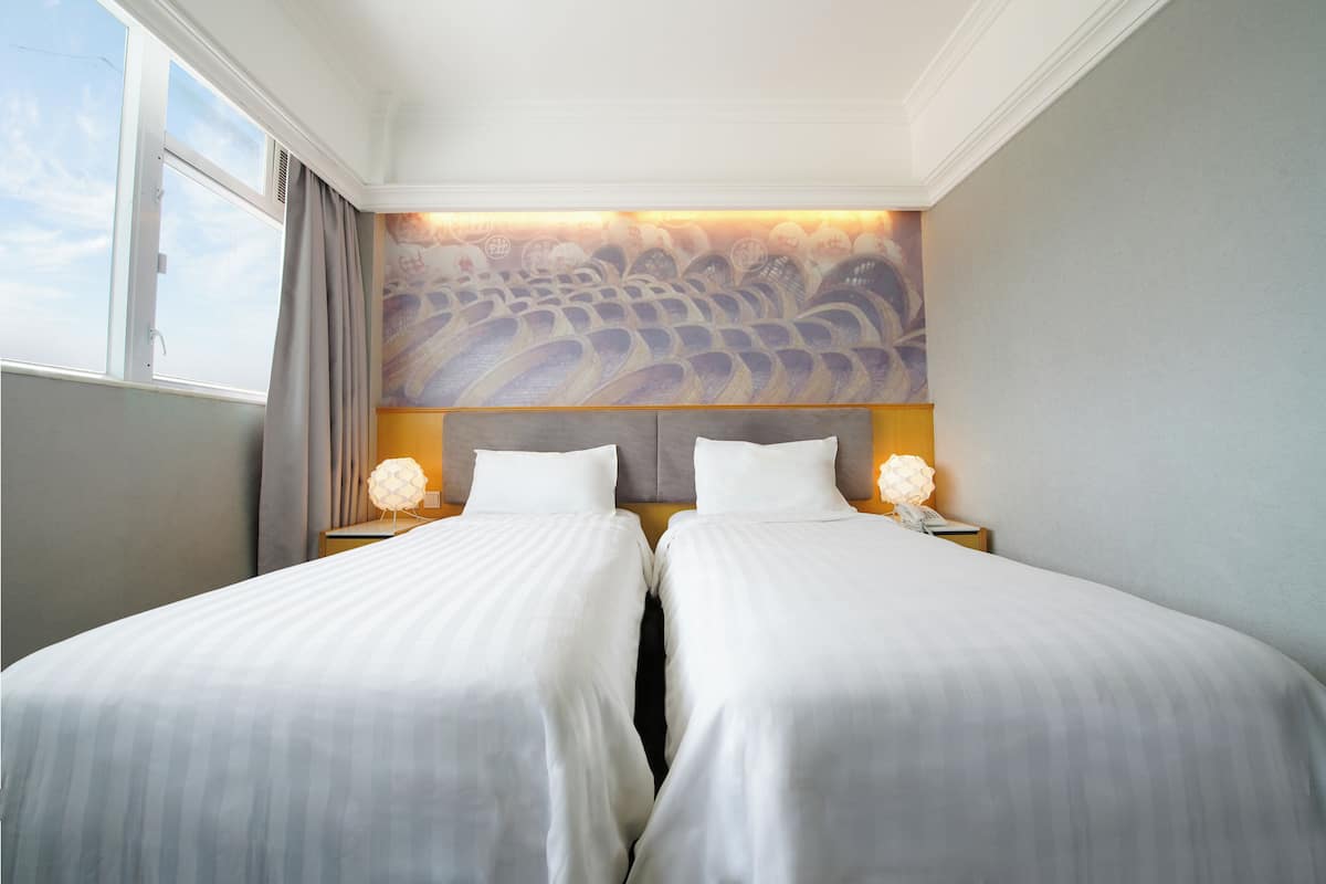 Quarto de hotel com duas camas, uma janela grande e um mural decorativo na parede.
