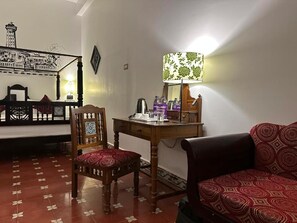 Quarto com escrivaninha de madeira, uma cadeira, sofá, luminária e cama com cabeceira estampada.