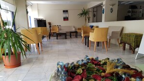 Um quarto espaçoso com uma grande planta em vaso, um espaço de refeições com cadeiras amarelas e uma mesa com toalha verde.
