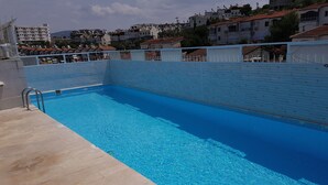 Piscina azul clara com deck ladrilhado e grades de metal, cercada por edifícios residenciais.