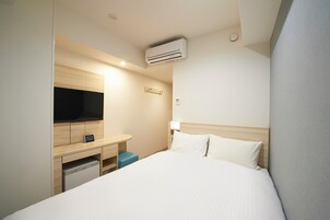 Quarto de hotel com cama, escrivaninha com televisão de tela plana, um pequeno espaço de estar e ar condicionado.
