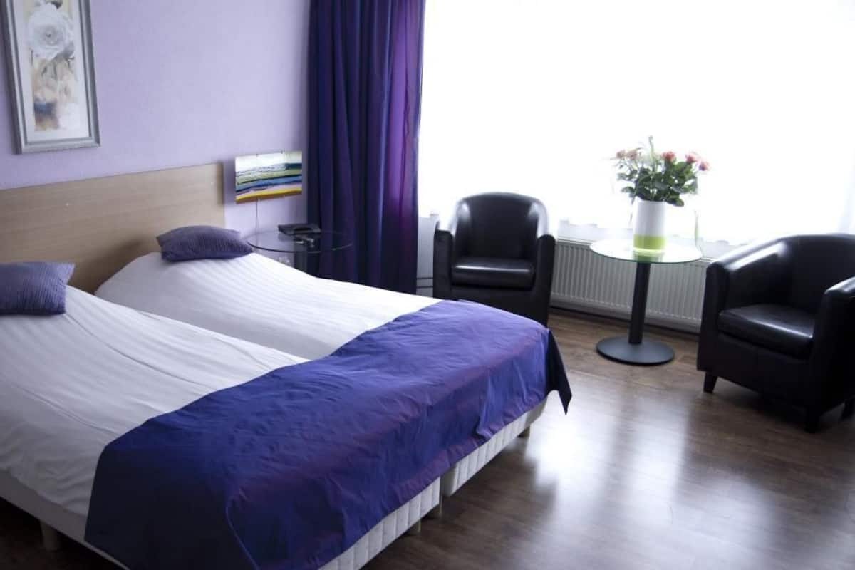 Quarto de hotel com duas camas, uma mesinha com um vaso de flores e duas cadeiras.