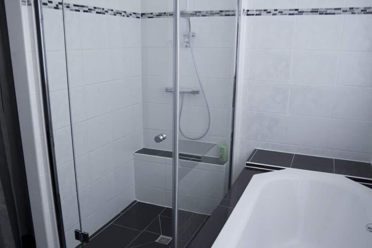 Um banheiro moderno com chuveiro em box de vidro, banheira branca e piso revestido.