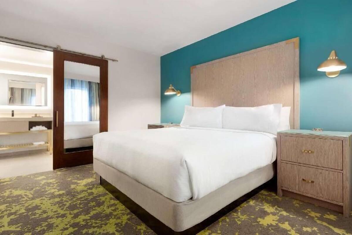 Quarto de hotel com cama, mesas de cabeceira, um espelho e vista para um banheiro.