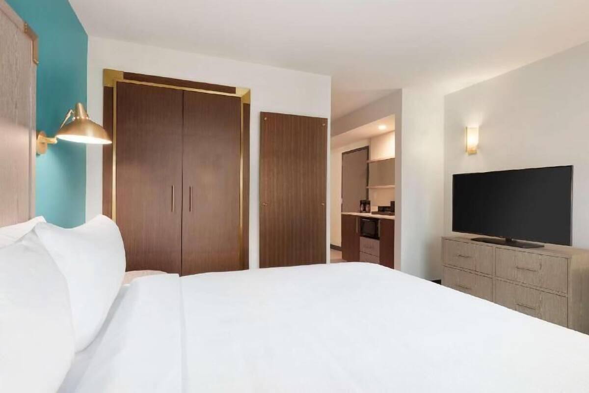 Quarto de hotel com cama, televisão, guarda-roupa e kitchenette.