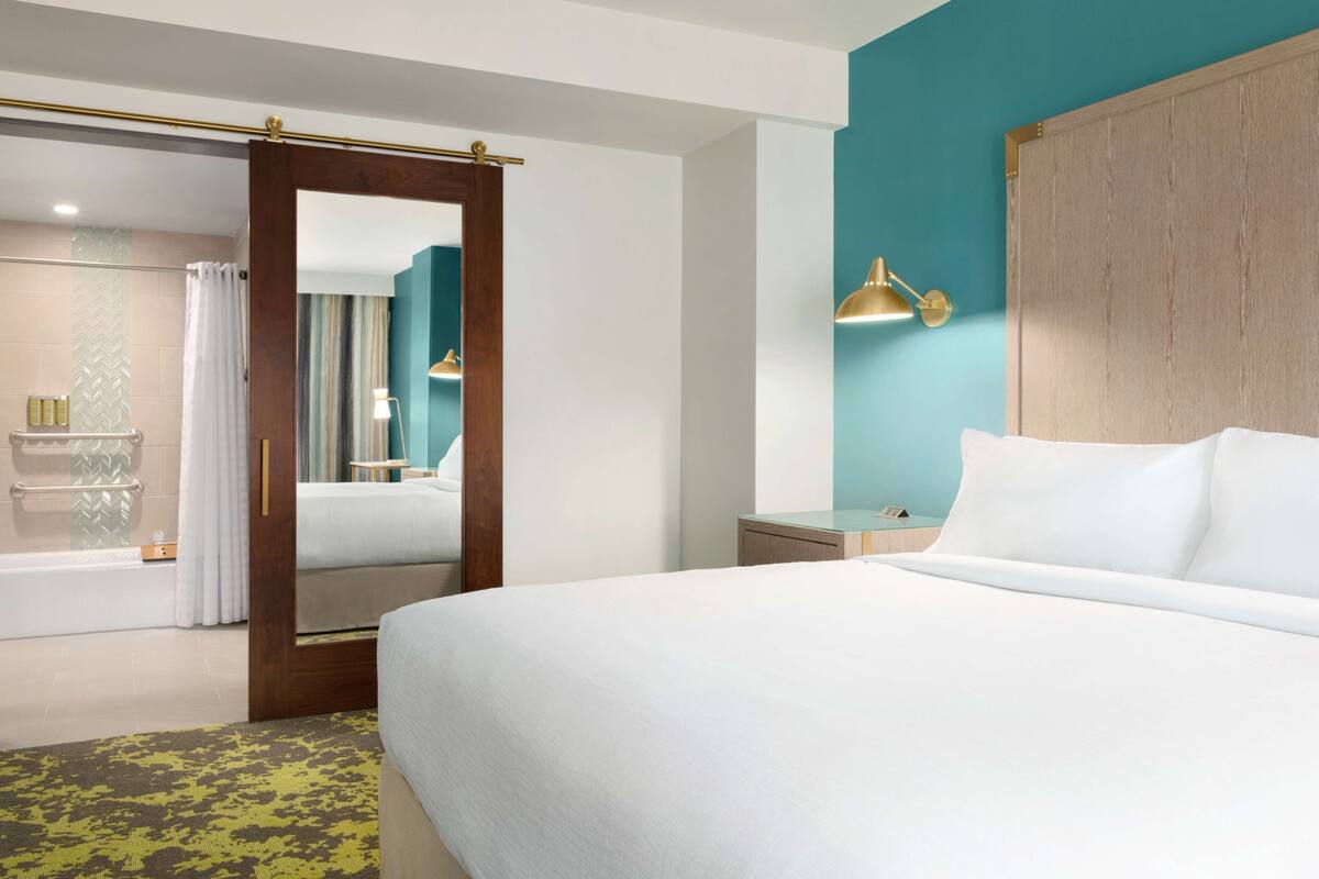 Quarto de hotel com uma cama grande, um guarda-roupa de madeira, casa de banho com chuveiro e um espelho.