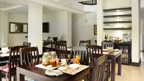Uma área de refeições com uma mesa de madeira posta para o café da manhã, cadeiras e uma cafeteira.