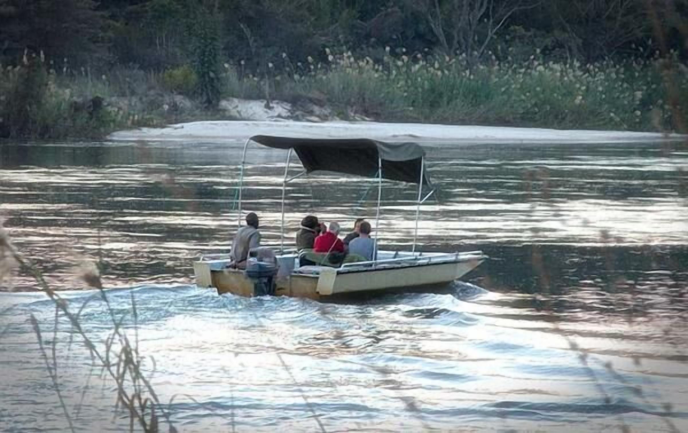 Um barco pequeno com toldo transportando três passageiros em um rio calmo.