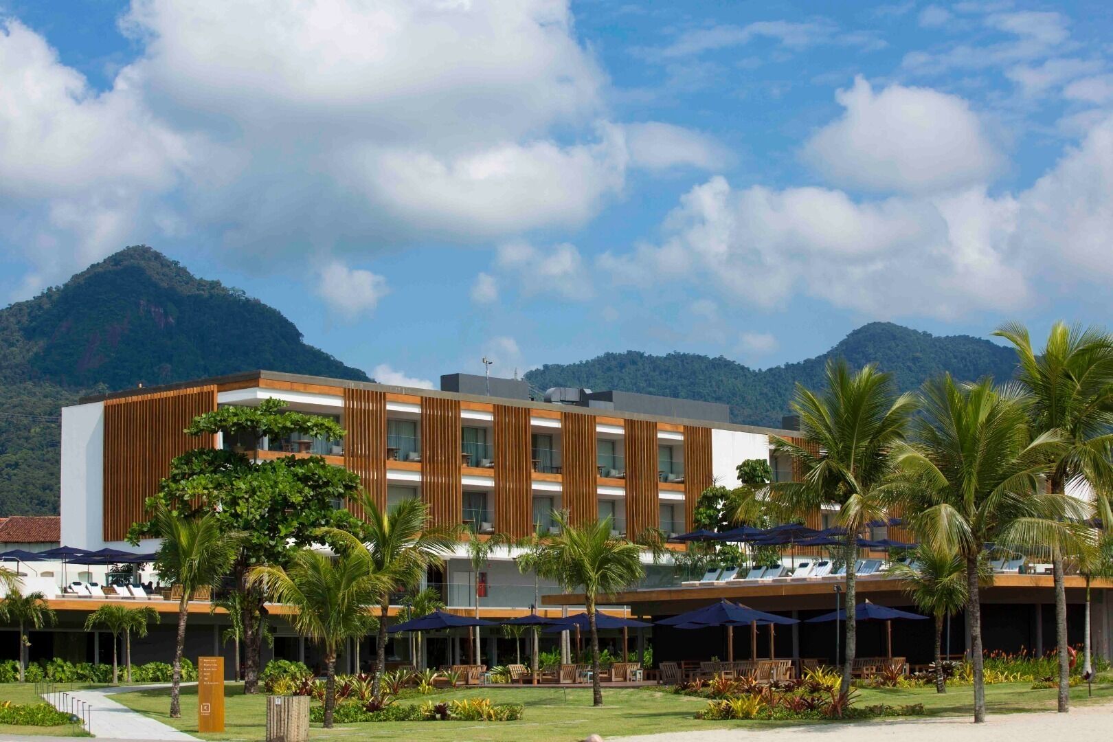 Um hotel moderno com estrutura em vários andares, área de estar ao ar livre e vegetação exuberante.