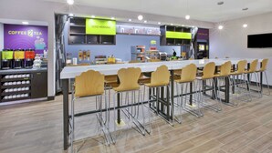 Um café moderno com um balcão extenso, várias máquinas de café e uma área de estar com cadeiras e mesas.