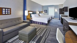 Quarto de hotel com sofá, duas camas, escrivaninha com televisão e uma janela grande.