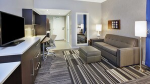 Quarto de hotel moderno com televisão de tela plana, sofá, escrivaninha e um espelho grande.