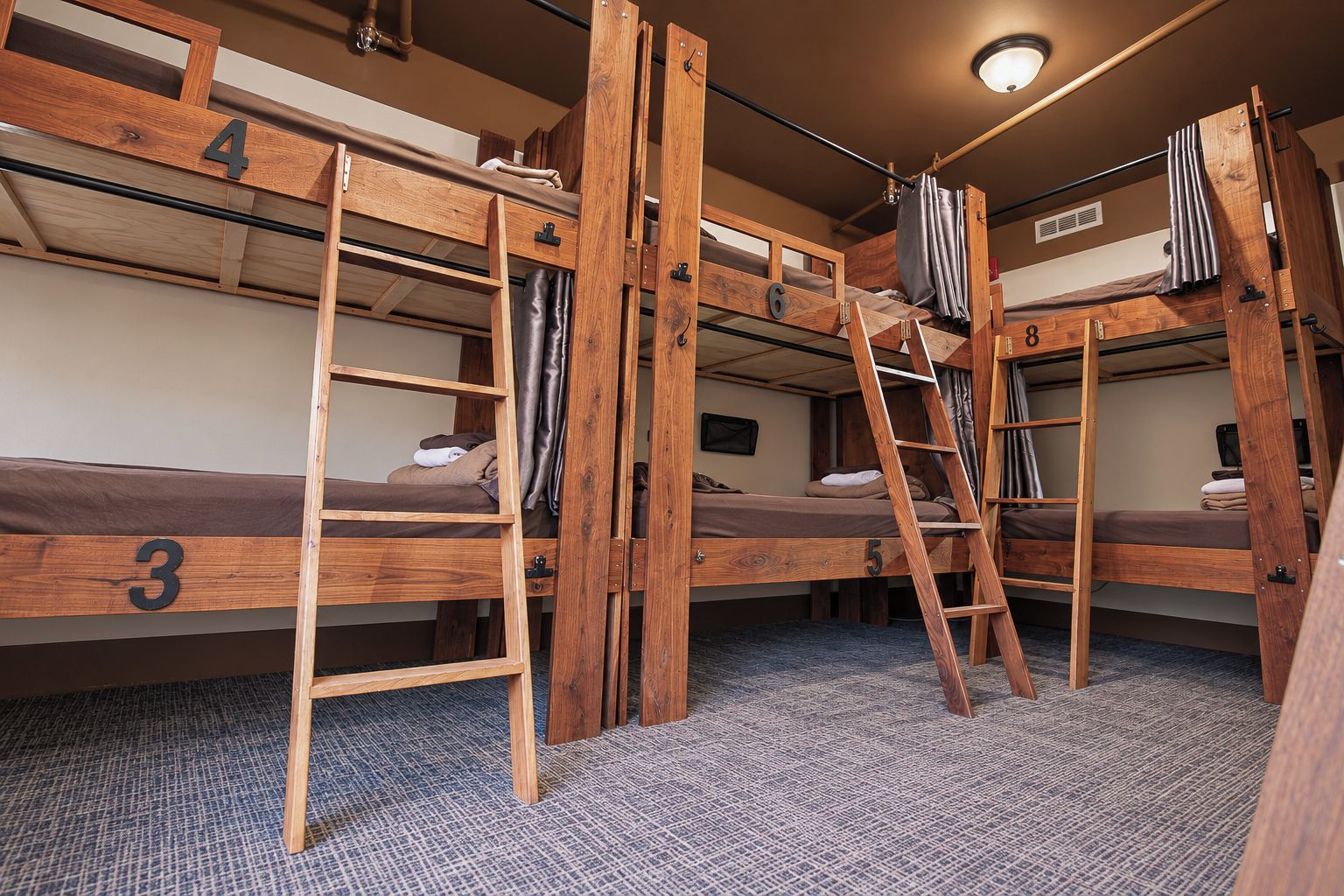 Quarto com beliches de madeira, camas numeradas e escadas.