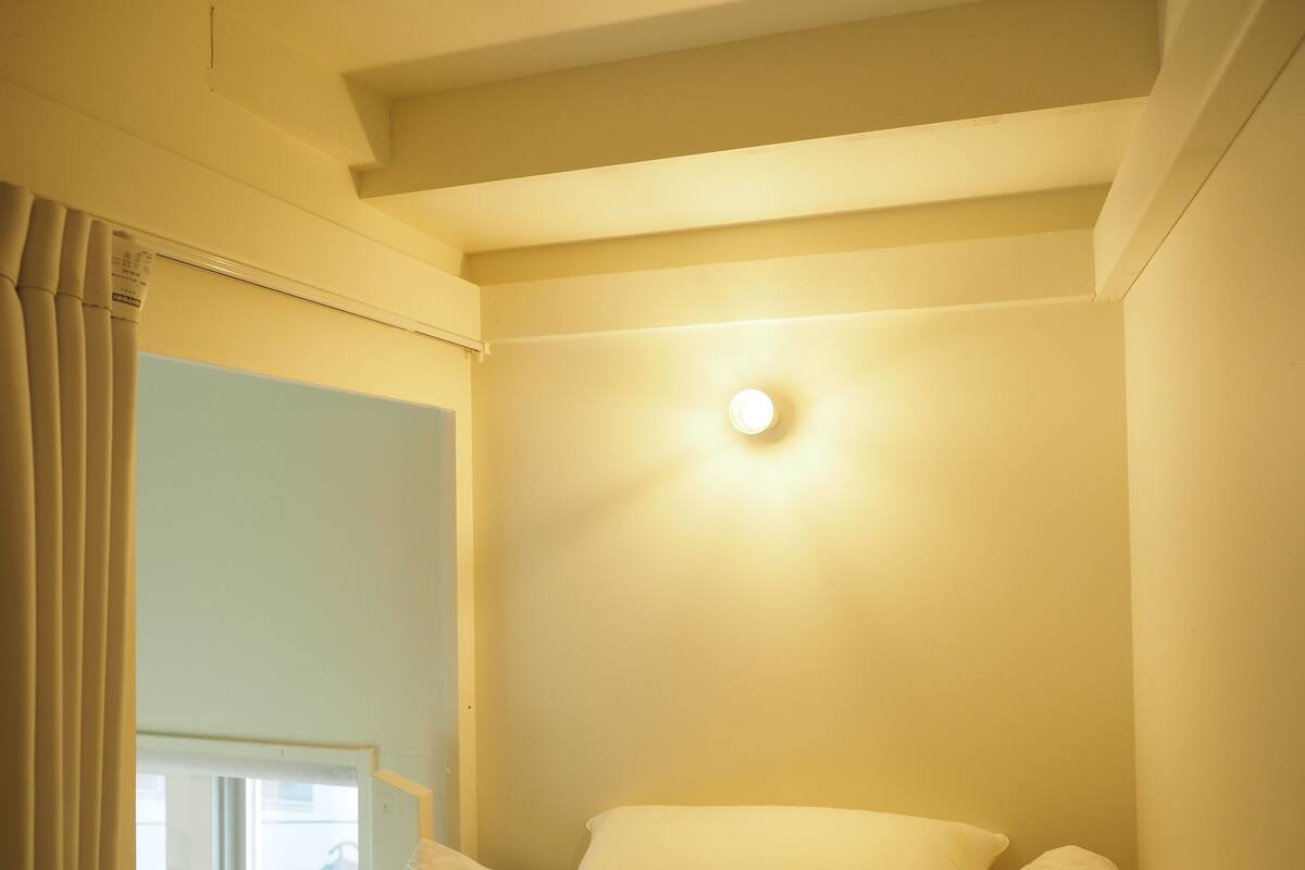 Quarto com cama, janela com cortinas e luminária na parede.