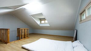 Quarto com teto inclinado, claraboia, cama e grades de madeira.