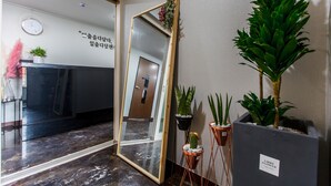Uma área de recepção com um espelho grande, plantas em vasos e um relógio na parede.