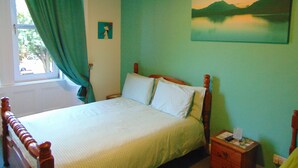 Um quarto com uma cama, mesa de cabeceira, pintura e janela com cortinas.