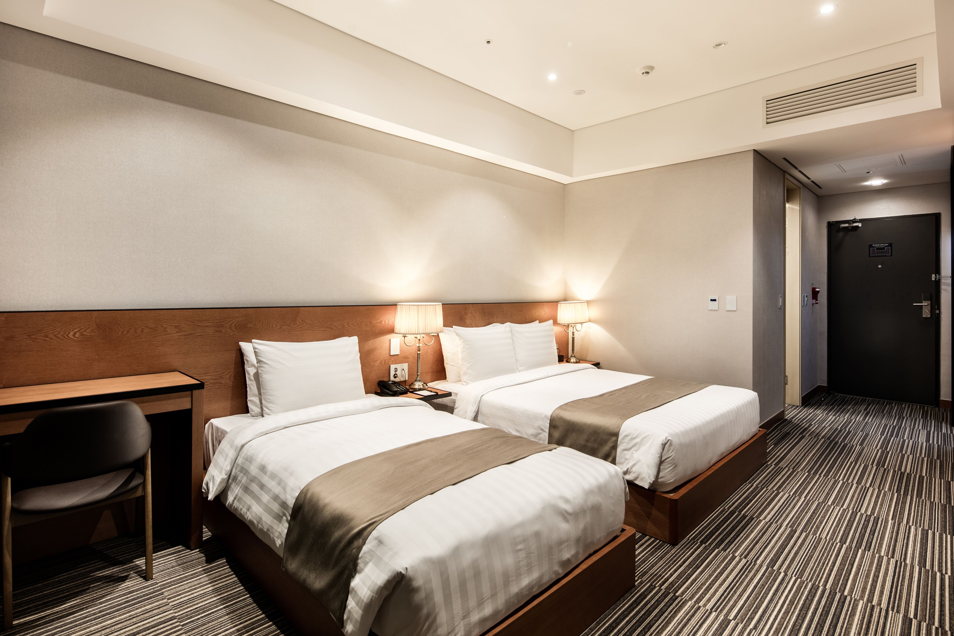 Quarto de hotel com duas camas, uma escrivaninha e uma cadeira.