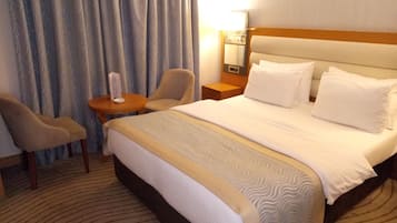 Quarto de hotel com uma cama grande, uma mesinha de cabeceira, uma cadeira e um abajur.