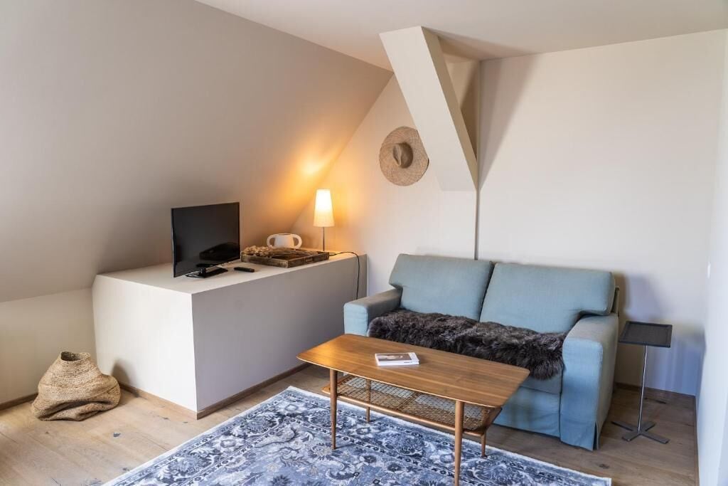 Uma sala de estar com sofá, mesa de centro, televisão em um suporte, luminária e um chapéu na parede.