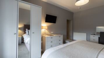 Quarto com cama, cómoda, mesa de cabeceira, abajur, televisão e guarda-roupa.